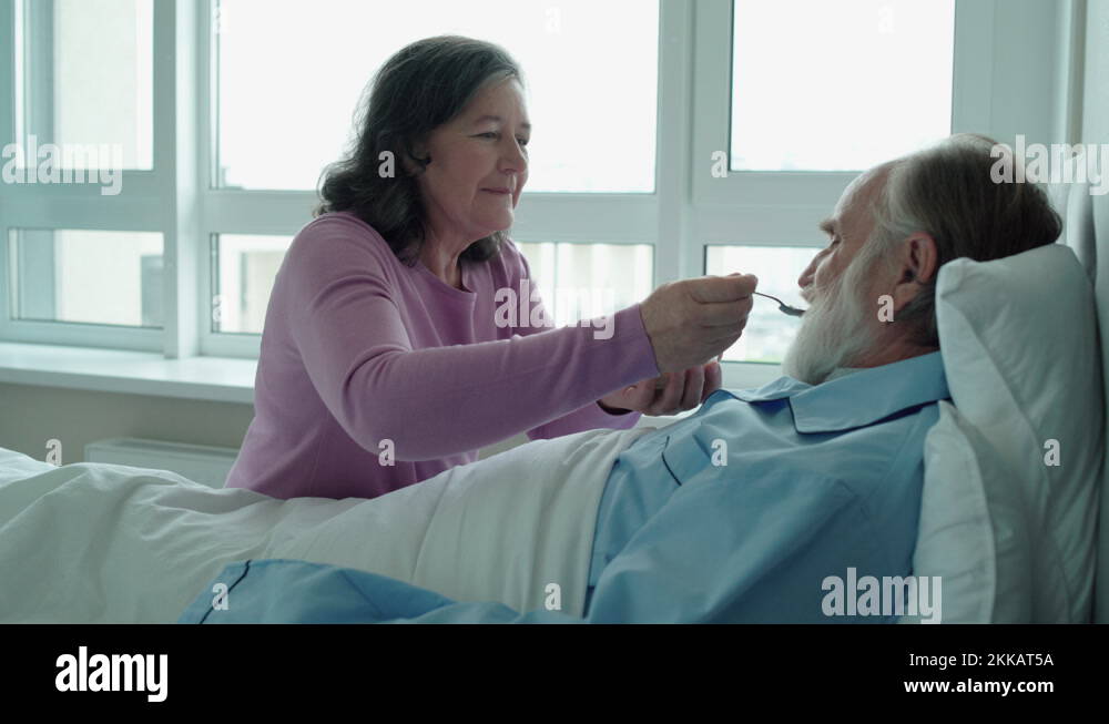 Caring wife feeding sick senior husband in bed, recovering from heart ...