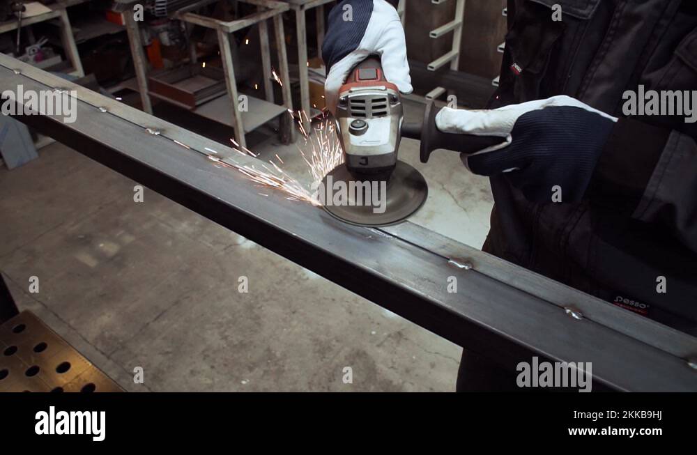 The worker is grinding metal beam with the angle grinder, there are a ...