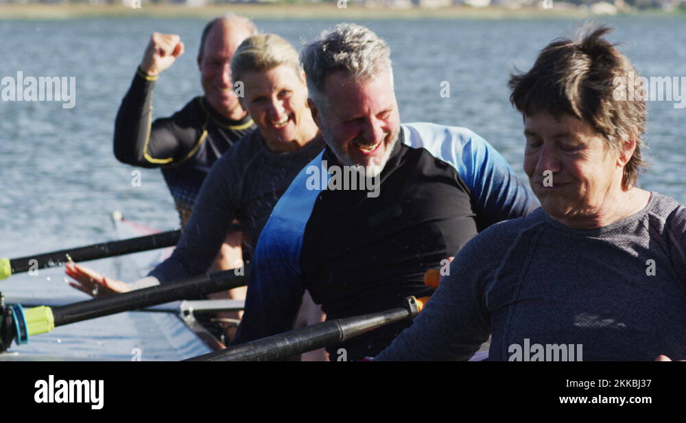Four senior caucasian men and women in rowing boat raising hands and ...