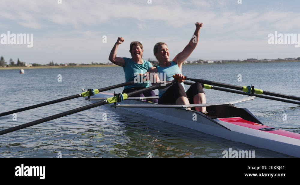 Two senior caucasian women in rowing boat raising hands and cheering ...