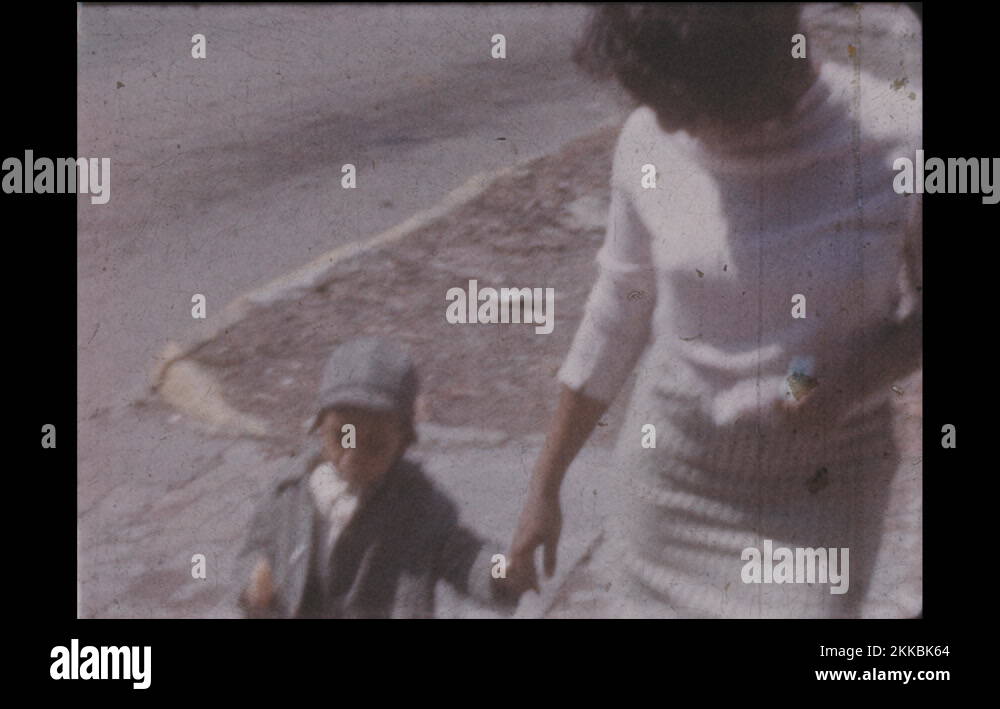 1960s: View of street, people talking on stoop. Boys on sidewalk. Woman ...