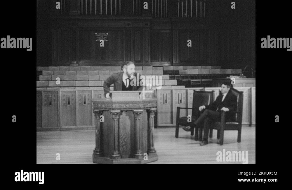 1960s: Man leans on lectern and speaks to classroom. Boy leans back and ...