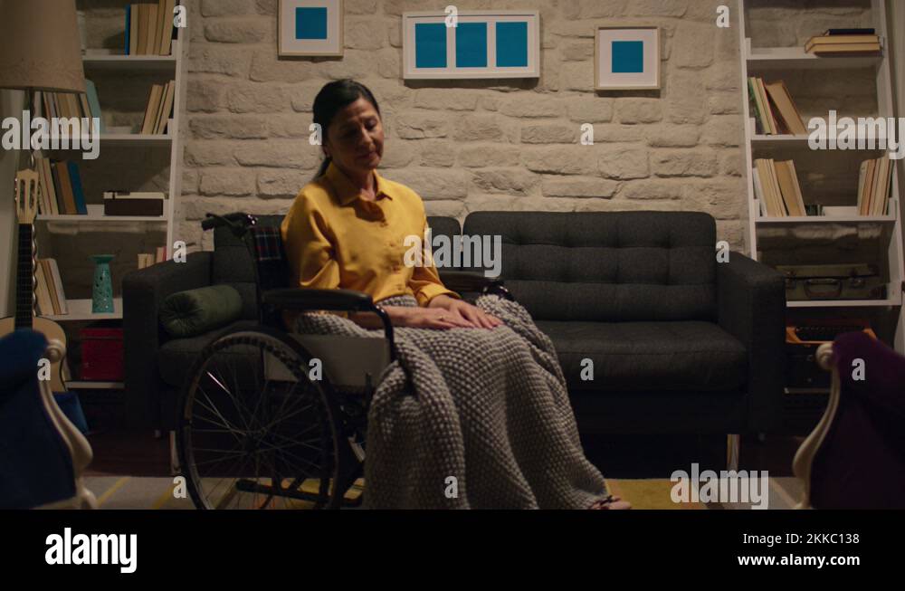 Sad disabled old woman sitting in a wheelchair alone in the living room ...
