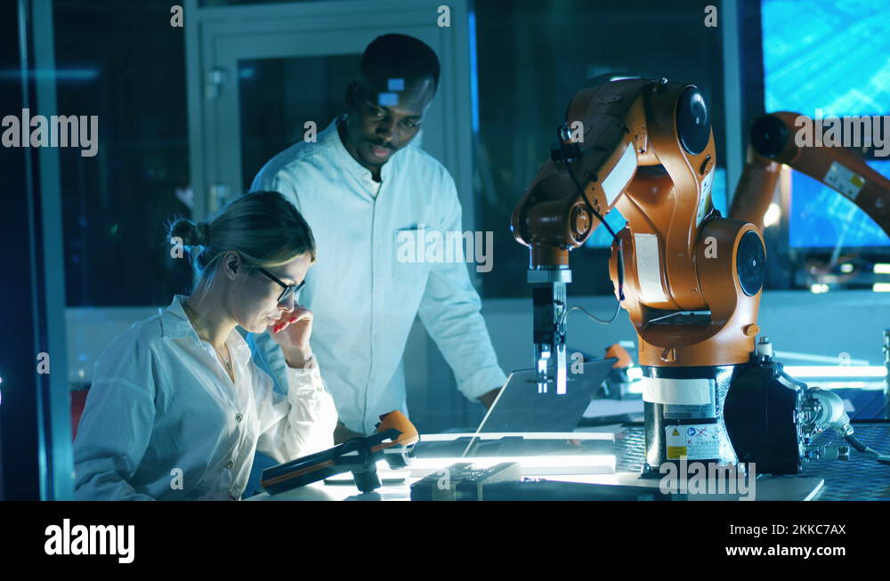 Two researchers in a science lab studying a robotic arm, industrial ...