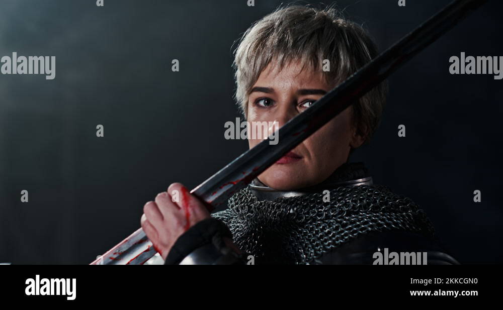 A brave female warrior with a sword in her hands looks into the camera ...