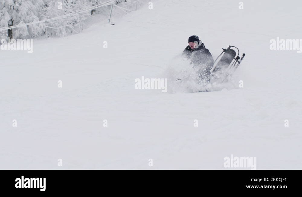 Young man sleds down a snowy slope. The sled rolls over and he falls ...
