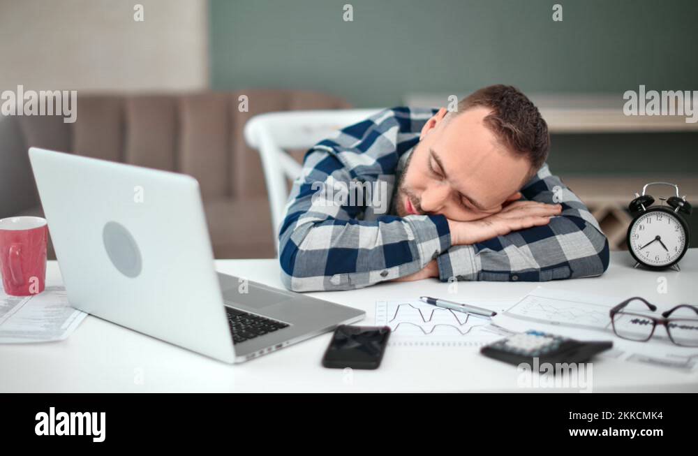 Man sleeping on desk at workplace surrounded by paper documents laptop ...