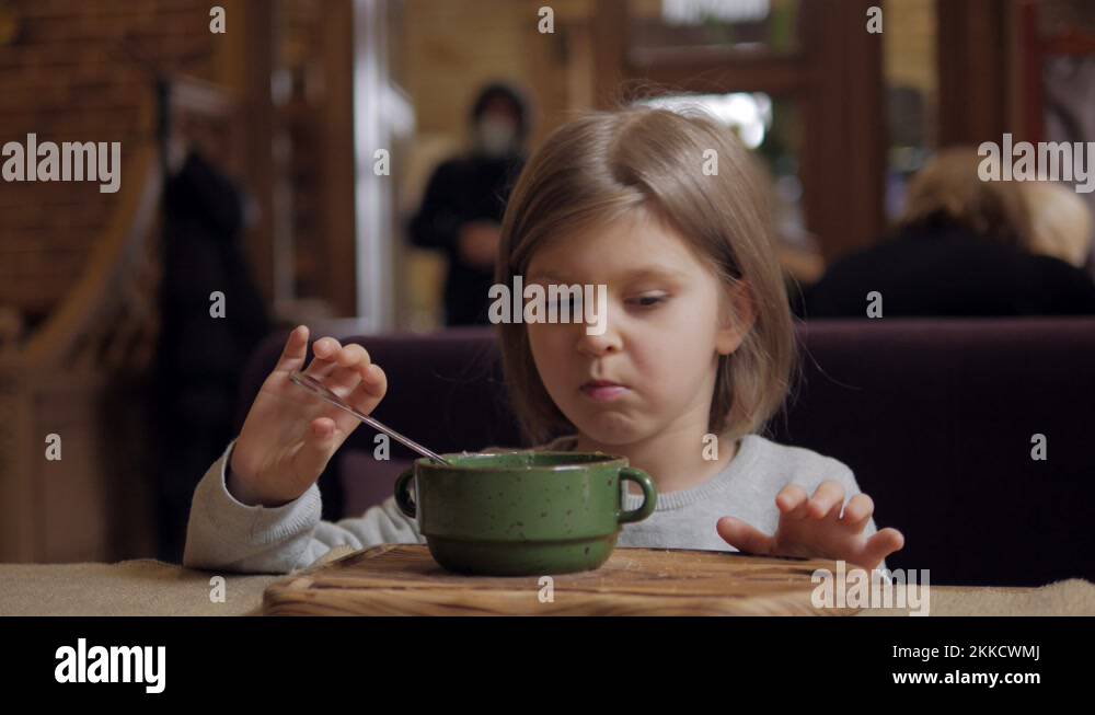 Little girl at the table in a restaurant eating soup. A visitor enters ...
