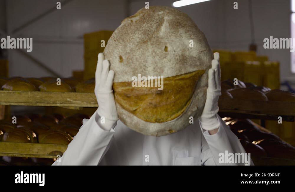 Baker in uniform raises a large loaf of bread with image of smile at ...