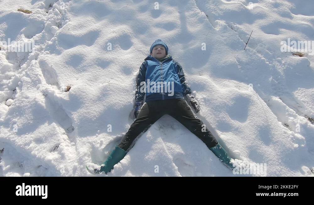 A young boy falling backwards in the fresh snow and making a snow angel ...