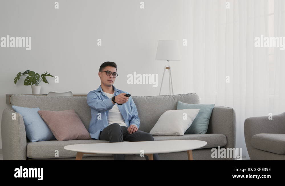 Young boring man in glasses switching channels on tv with remote controller and Stock Video ...