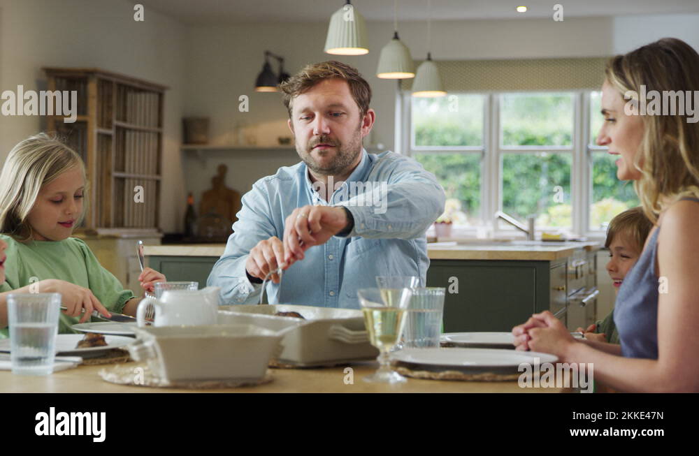 Father Serving Food As Family Sit Around Table At Home Enjoy Meal ...