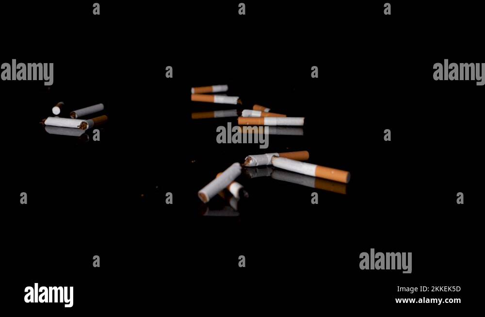 Throwing cigarettes stubs on black reflective background from the right ...
