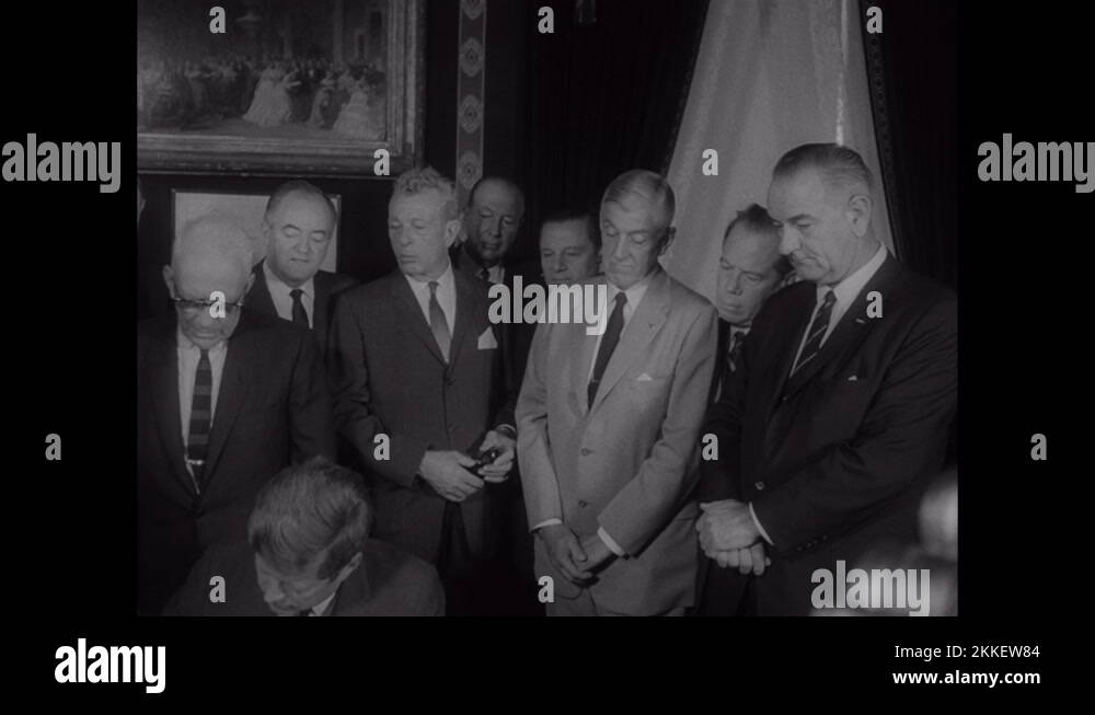 1960s: John F Kennedy signs paper at desk as flashbulbs go off, Lyndon ...