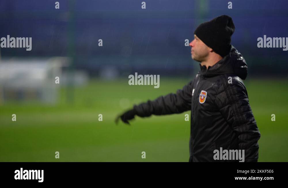 Football team coach in rain cheering team, waves his hands and controls ...