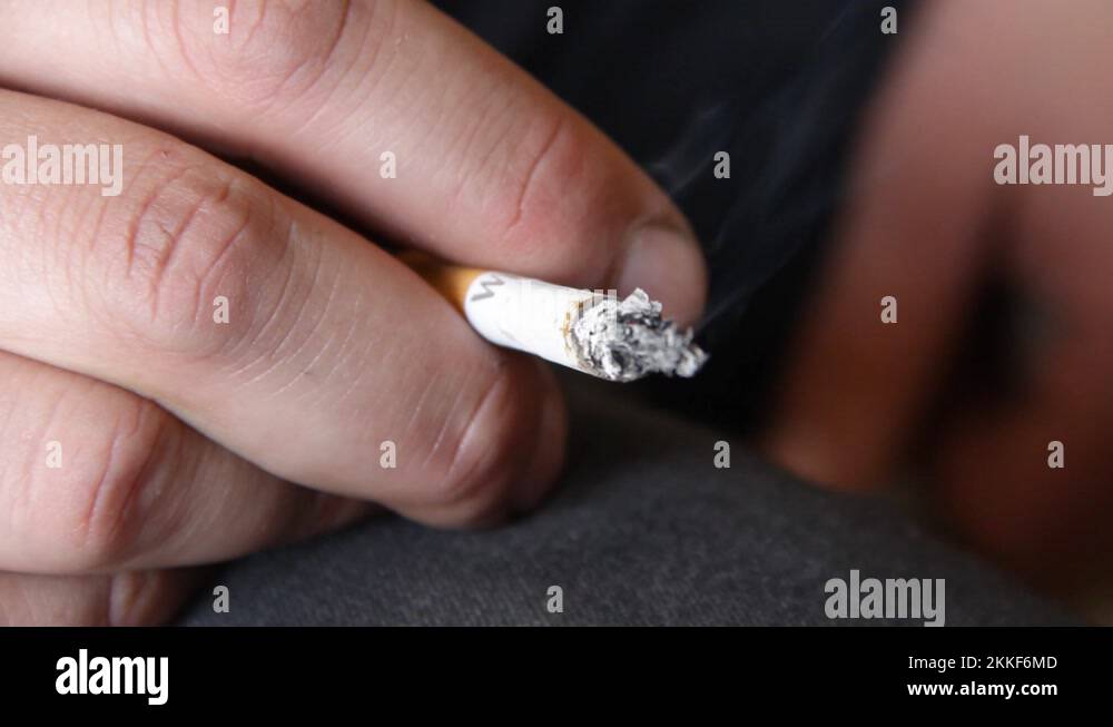 Cigarette smoking in the fingers of a young adult mans hand. White ...