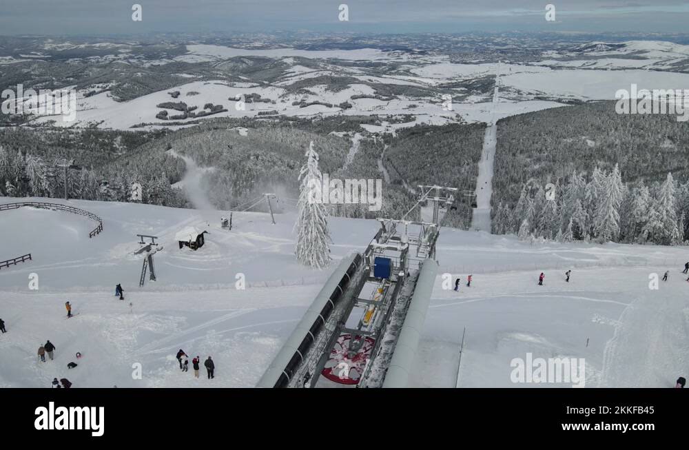 Top of ski mountain. Ski lifts, gondola and people skiing. Trees and ...