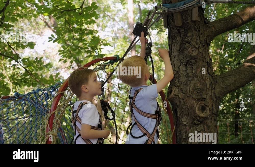 Two little boy in climbing gear is walking along a rope road in a Park ...