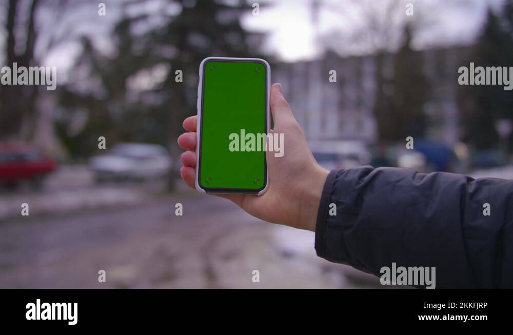 Hand man uses holding a mobile telephone with a vertical green screen ...