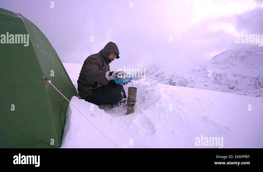 A man boiling water while camping in snow in the highlands mountains ...