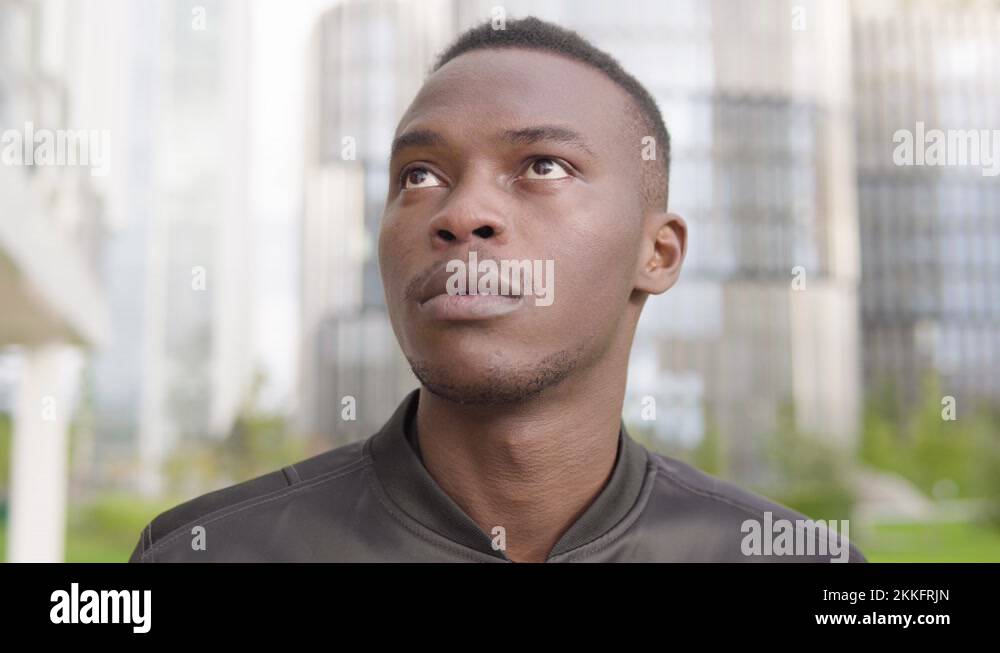 A young black man looks around - face closeup - office buildings in the ...