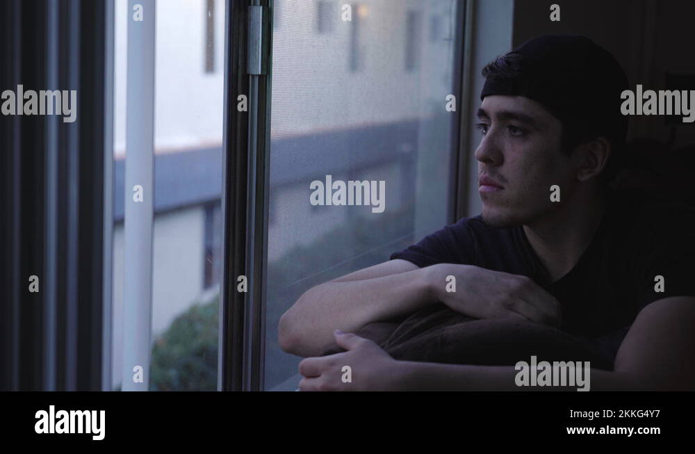 A depressed man dramatically looking outside of the window in his Stock ...