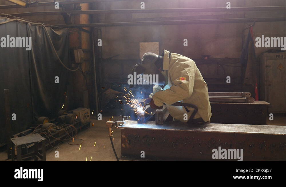 Worker welds metal parts. Masked welder in the workplace. Fying sparks ...