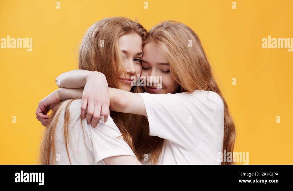 Love of sisters. Two similar twins embracing over orange studio ...
