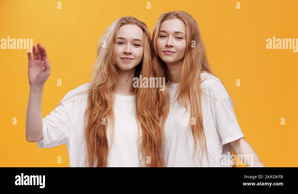 Greeting. Two young friendly redhead twin sisters waving hands hello to ...