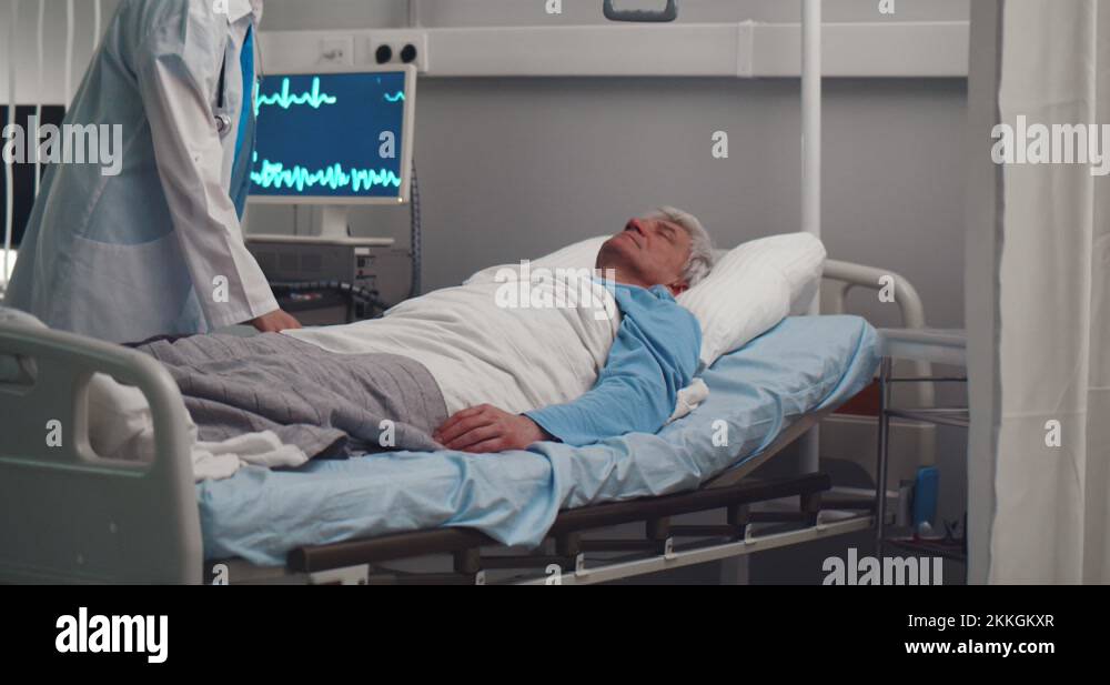 Female doctor checking pulse of aged male patient sleeping in bed at ...