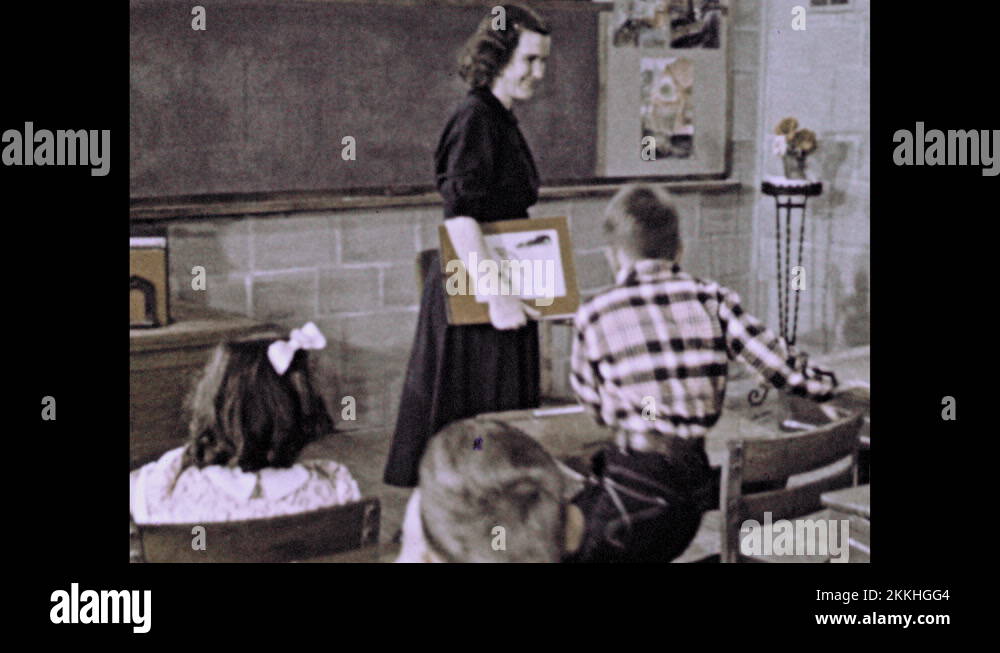 1950s: Children enter classroom and sit in desks. Teacher at front of ...