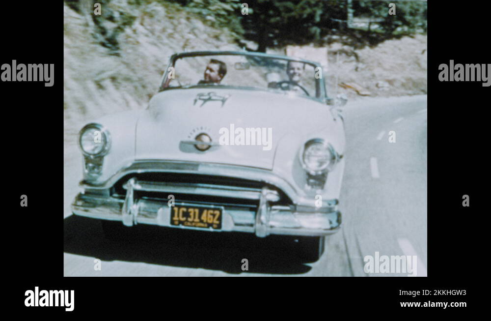 1950s: Two men ride in convertible down road. Men follow woman driving ...