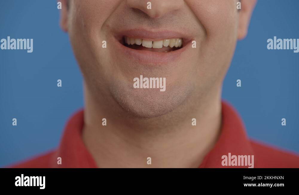 Close-up serious young man mouth smile in front of the blue background ...