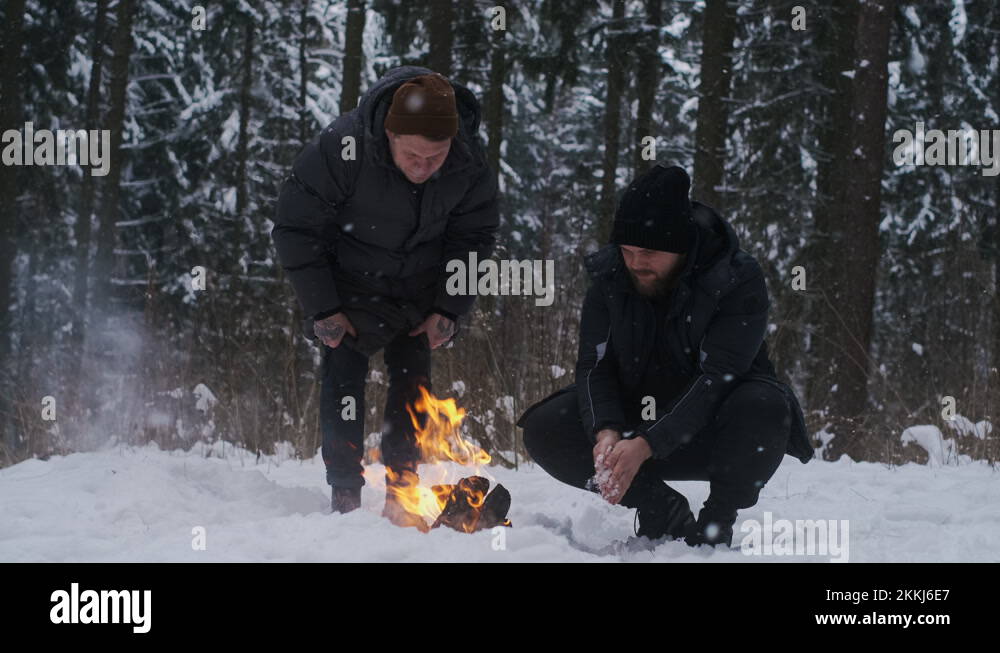 Two friends enjoy the fire at camping in the winter woods, making a ...
