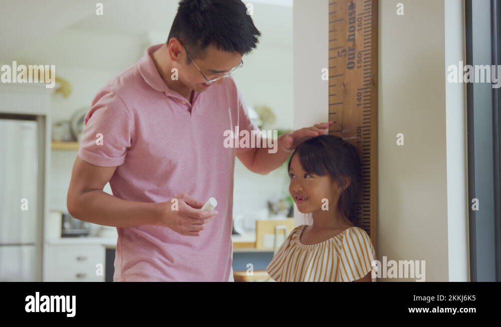 Asian Father Measuring Daughter On Wall Scale At Home As She Stands On ...