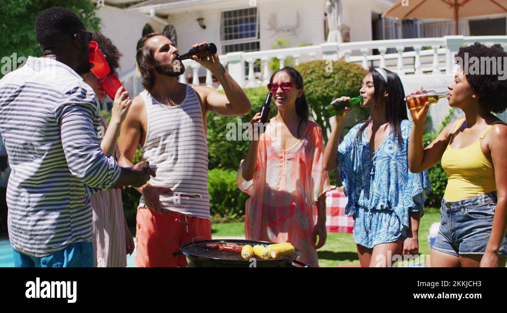 Diverse group of friends having barbecue and drinking beer at a pool ...