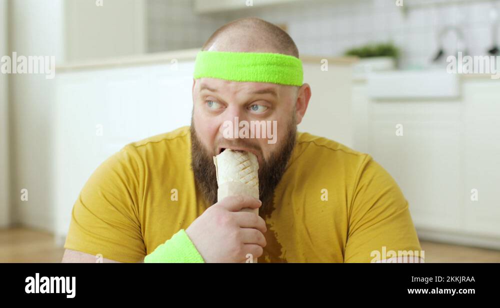 Portrait of sweaty fat man in yellow wet sportswear is eating danar in ...