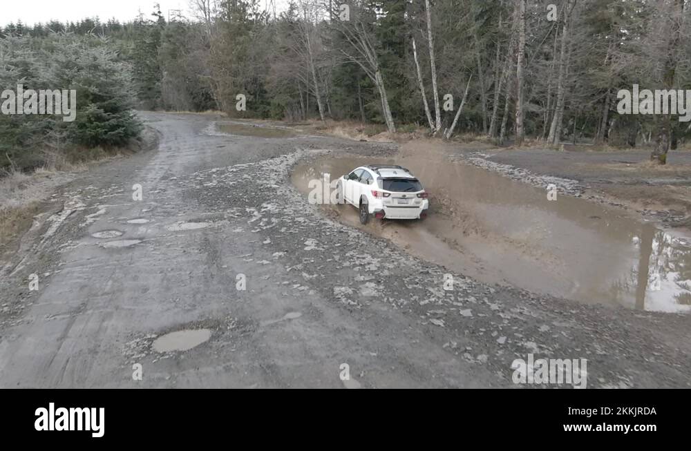 A single white Subaru Crosstrek drives into a deep mud puddle splashing ...