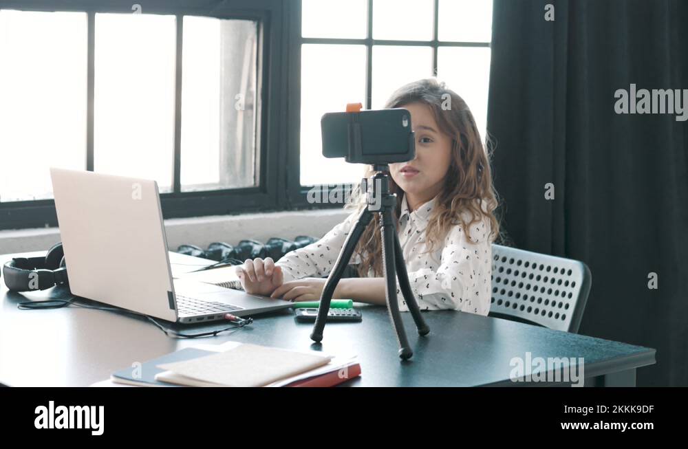 Kid girl having livestream with phone and tripod at modern office like ...