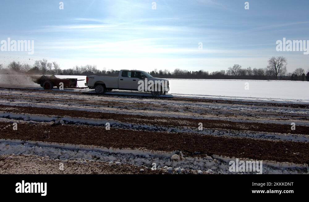 Manure Spreader Is Being Pulled By A White Pick-up Across The Winter ...
