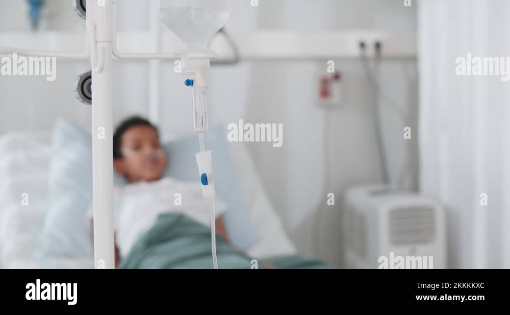 Focus on drip in hospital room with blurry patient child on hospital ...
