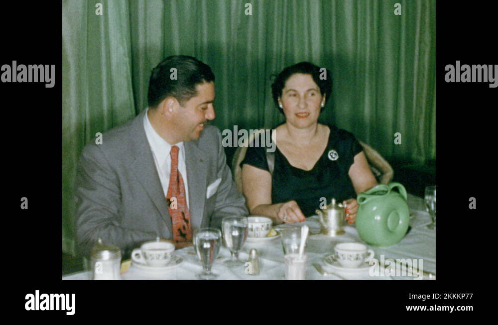 1950s: UNITED STATES: man smokes cigarette at party. People eat desert ...