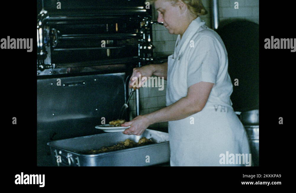1950s: Cafeteria workers prepare lunch in large kitchen. Man leans on ...