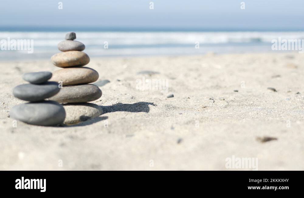 Rock balancing on ocean beach, stones stacking by sea water waves ...