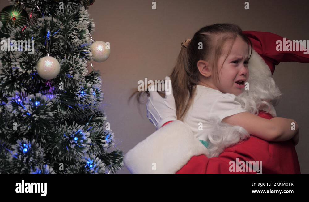 Little girl crying and hugging Santa Claus. The kid is upset Santa ...