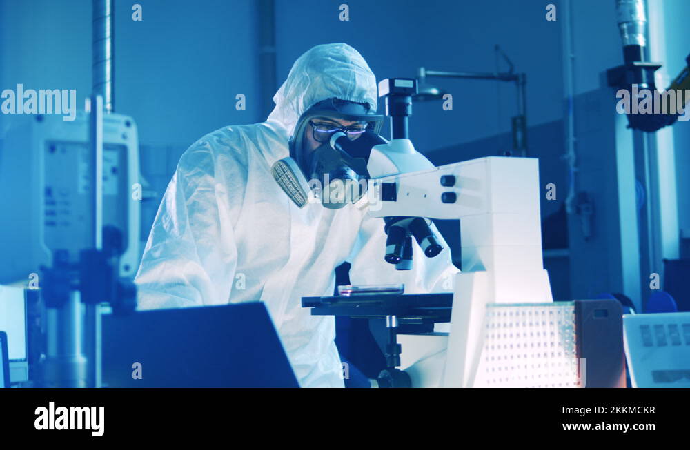 Laboratory worker in a splash suit is operating a microscope Stock ...