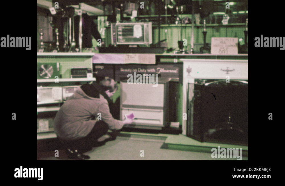 1960s: Store. Man checks price tag on heater. Man turns knob on air ...