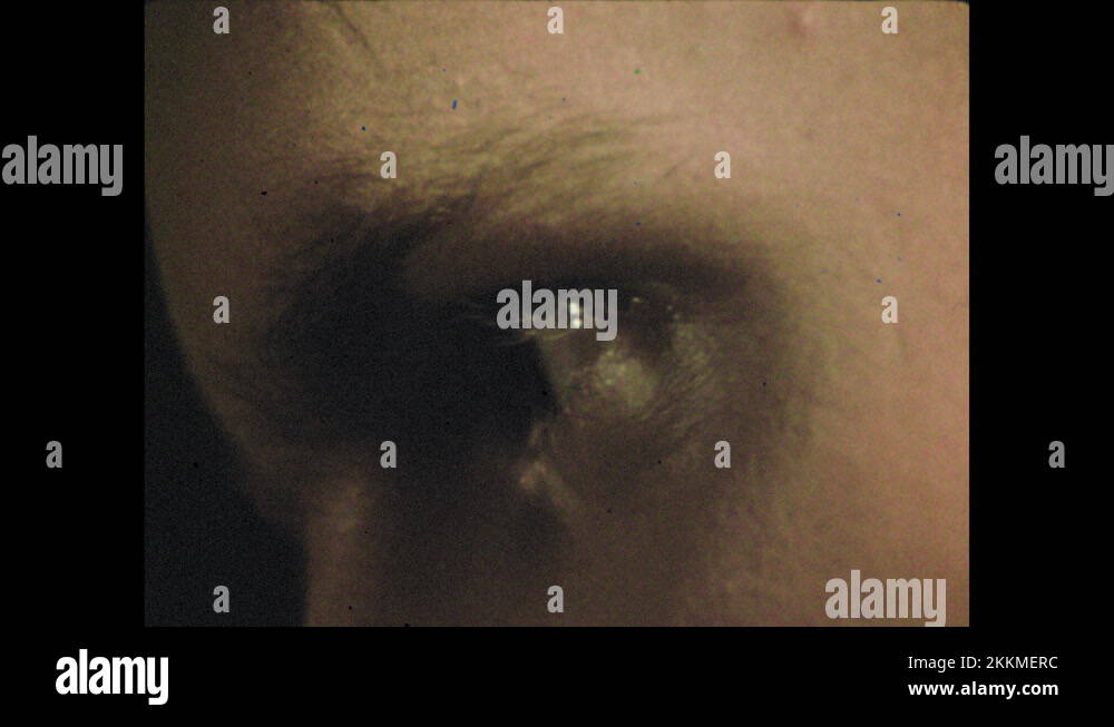 1960s: Man standing in front of door to house at night. Man's left eye ...