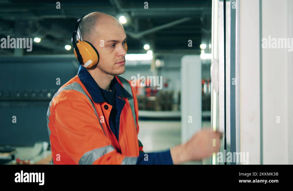 Bald male engineer operates a machine at a factory using a touchscreen ...