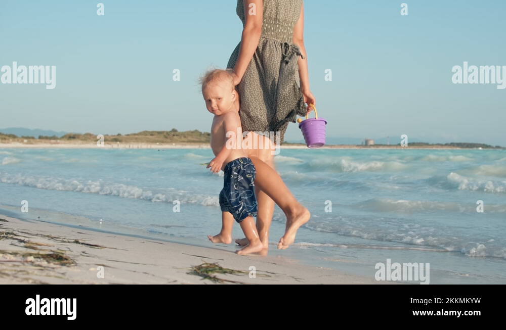Cute child looking around at seashore. Baby boy walking with mother at ...